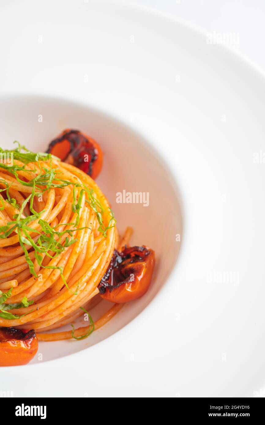 A bowl of spaghetti with burned tomatos and shredded basil Stock Photo ...