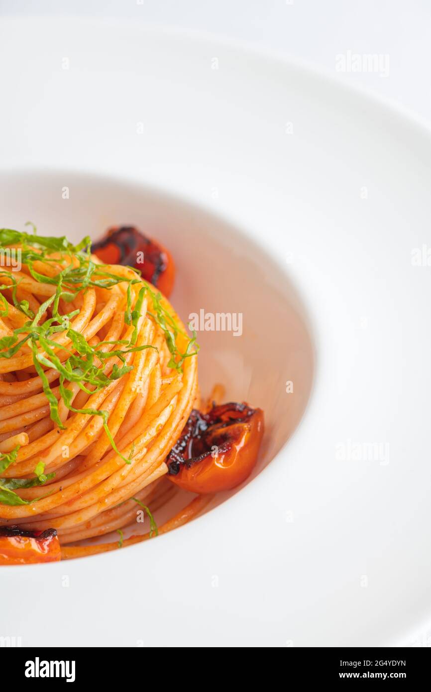 A bowl of spaghetti with burned tomatos and shredded basil Stock Photo ...