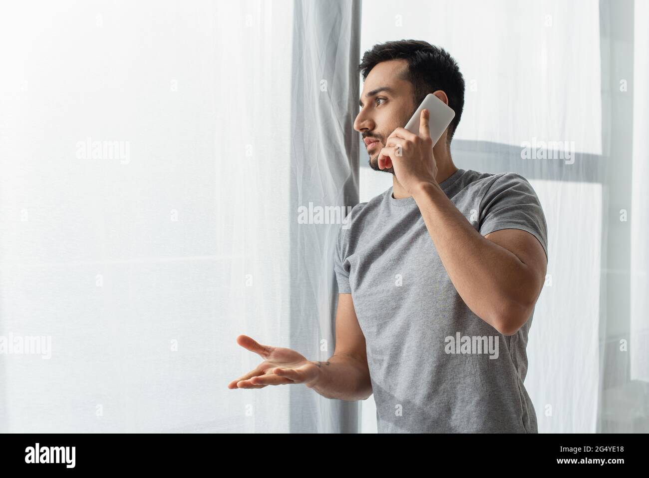 Side view of man pointing with hand while talking on smartphone near ...