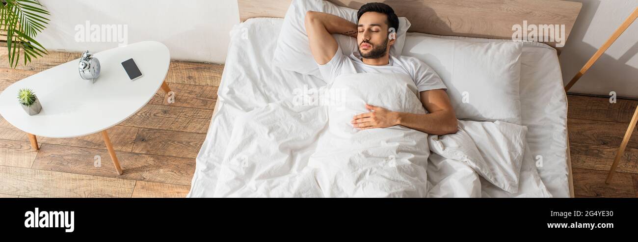 Top view of young man sleeping on bed near alarm clock and mobile phone ...