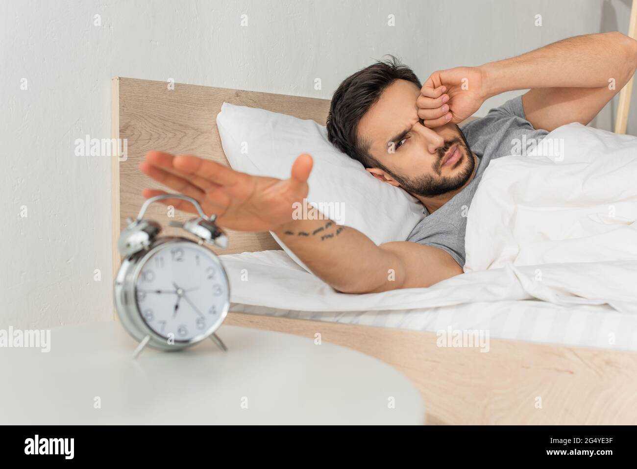 Young man pulling hand to blurred alarm clock while waking up Stock ...