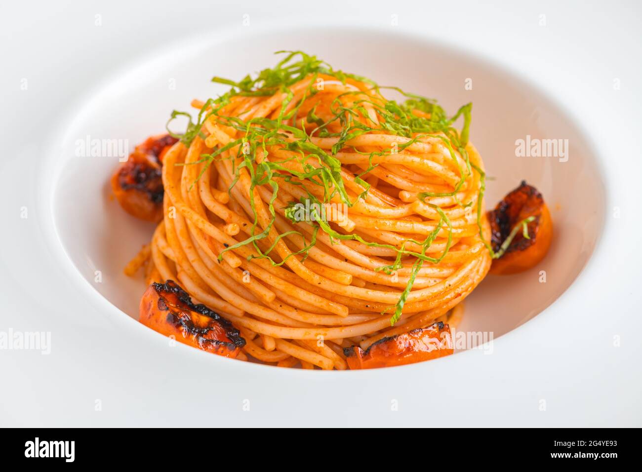 A bowl of spaghetti with burned tomatos and shredded basil Stock Photo ...