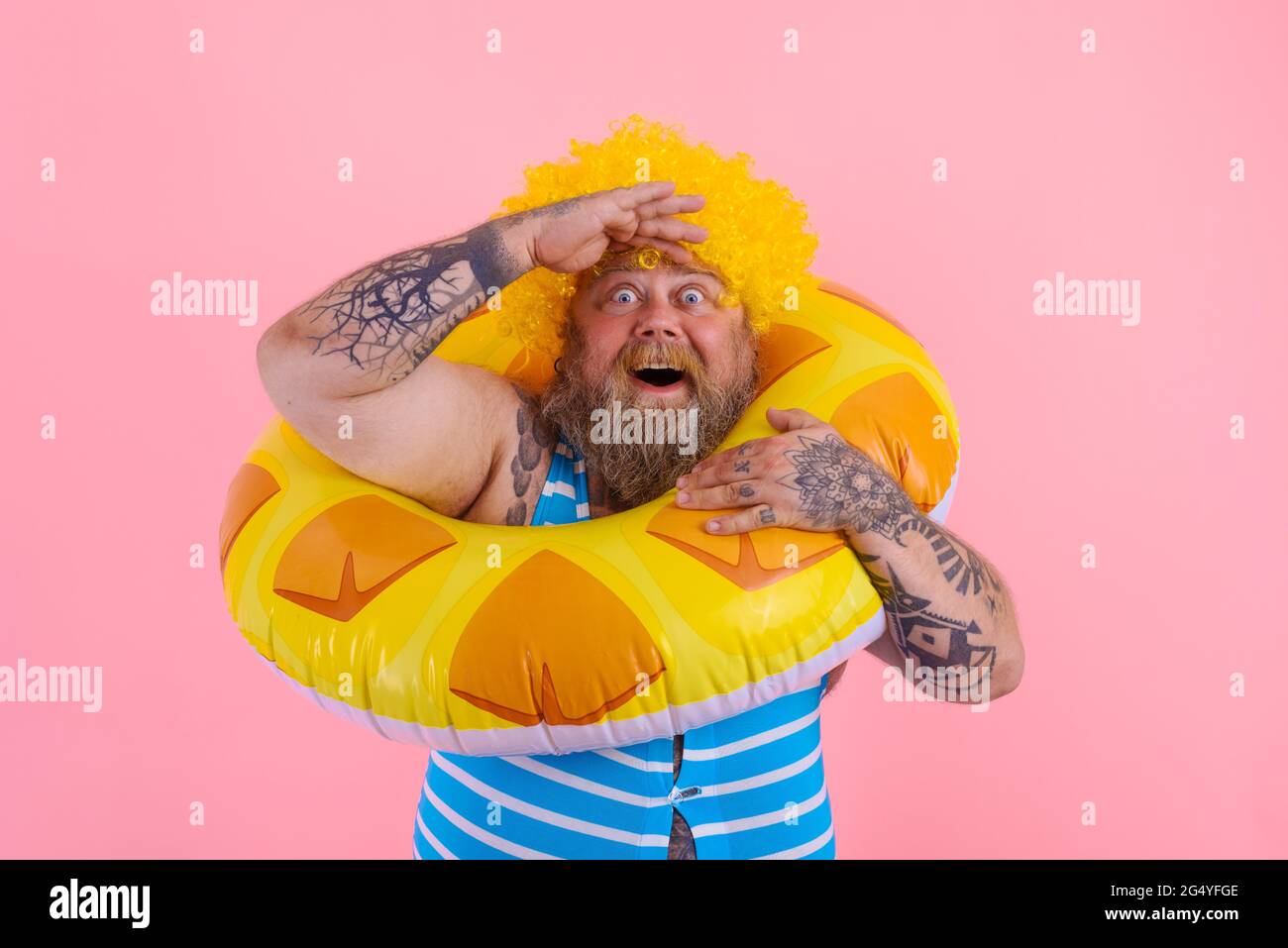 Fat amazed man with wig in head is ready to swim with a donut lifesaver ...