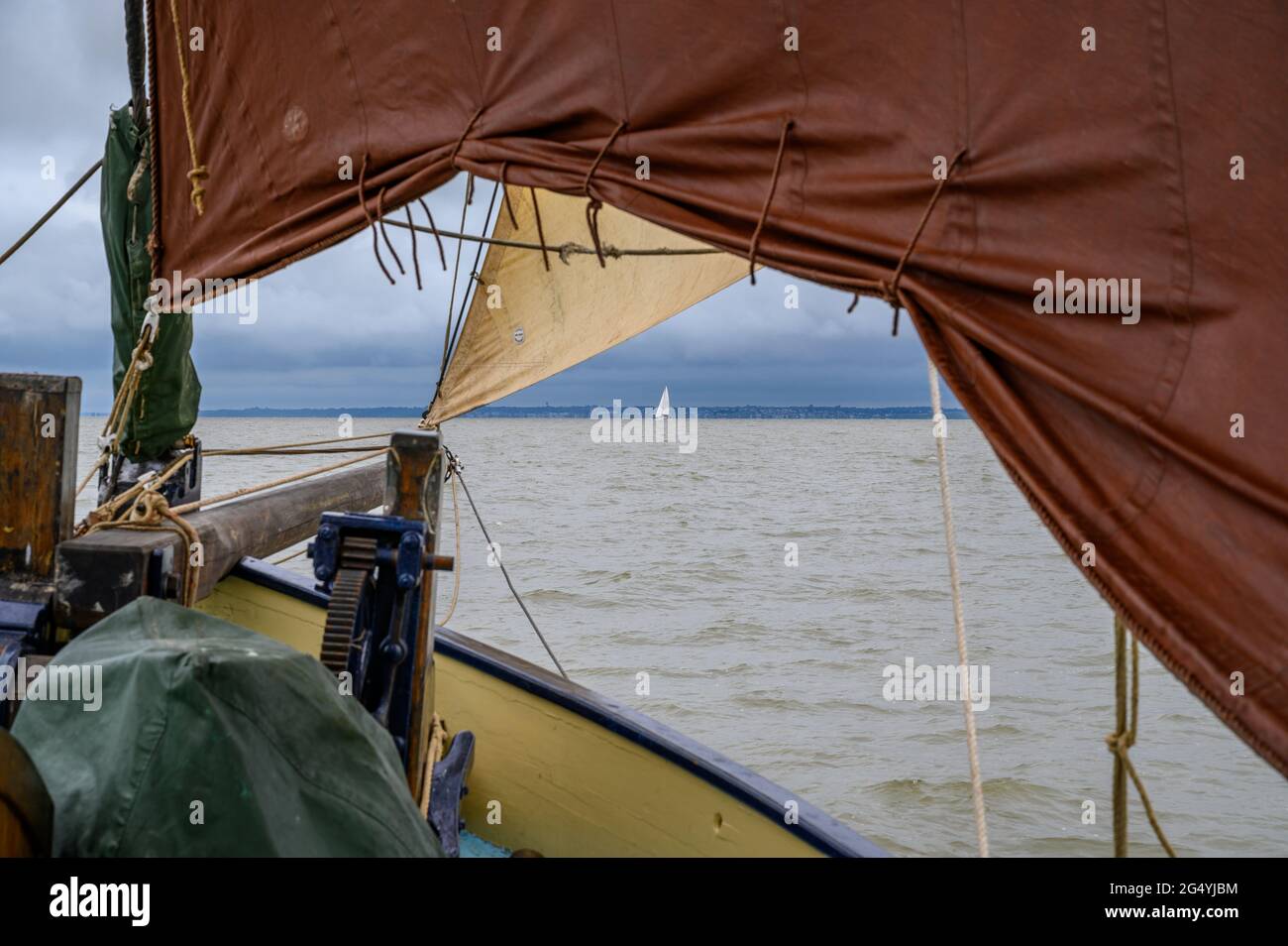 A distant sailboat seen from under the foresail and jib on the bow of ...