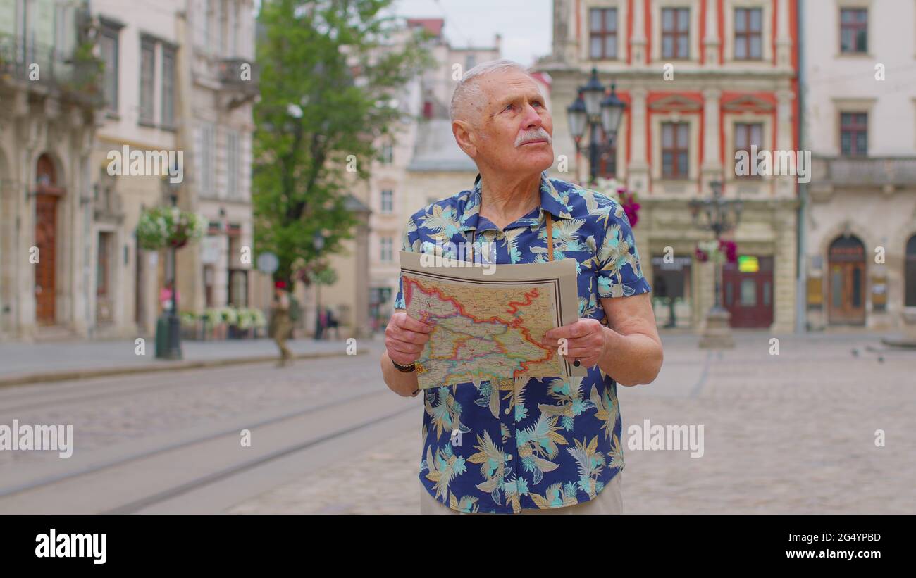 Elderly stylish tourist grandfather man walking along street looking ...