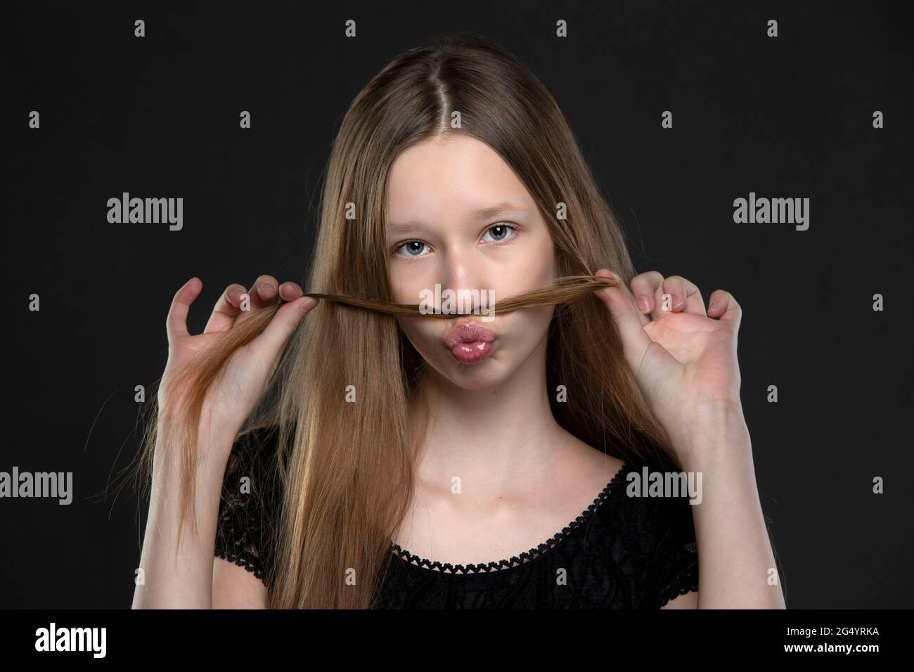 Beautiful teenage girl fooling around in front of the camera. She makes a mustache out of her ...
