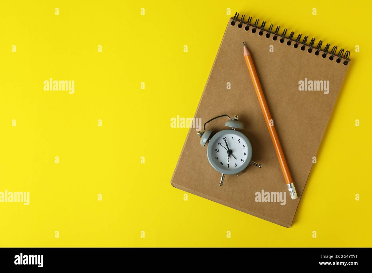 Alarm clock, notebook and pencil on yellow background Stock Photo - Alamy