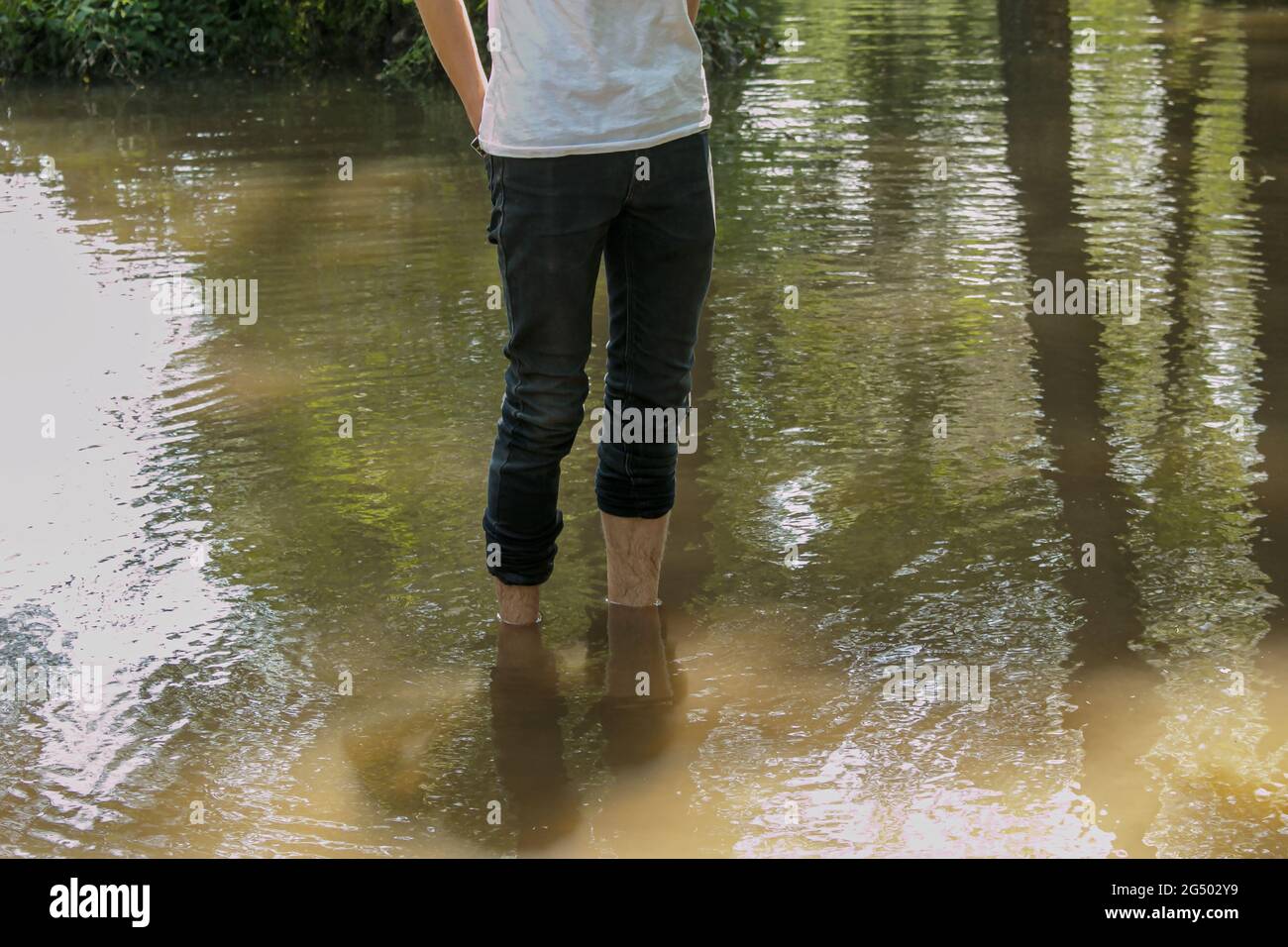 Male feet in the water in a flooded park, close-up. A young man stands ...