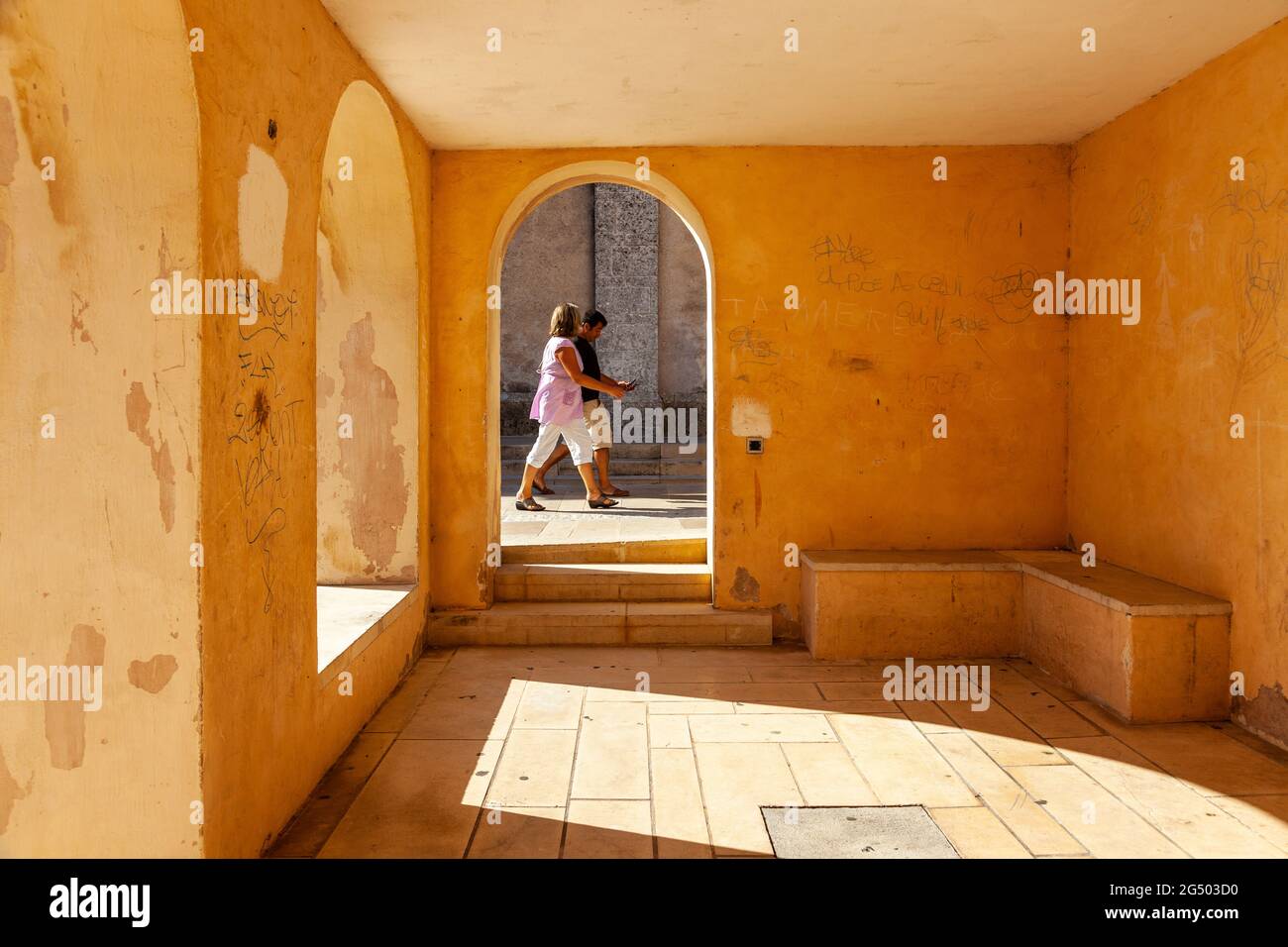 Shaded arcade in a street in Bonifacio. Yellow-orange walls; passers-by ...