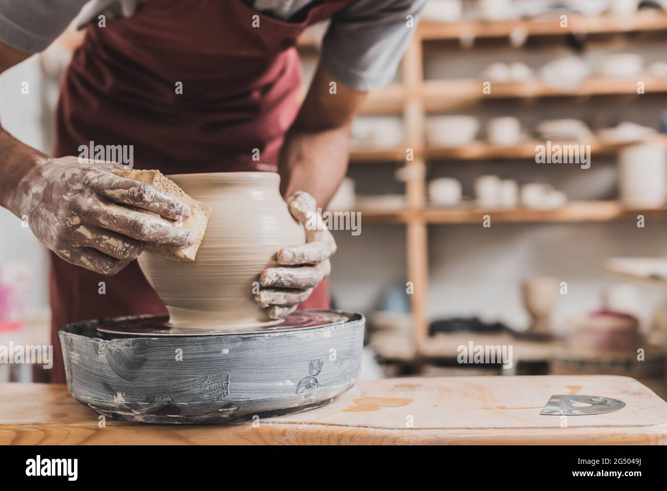 partial view of young african american man making wet clay pot on wheel ...