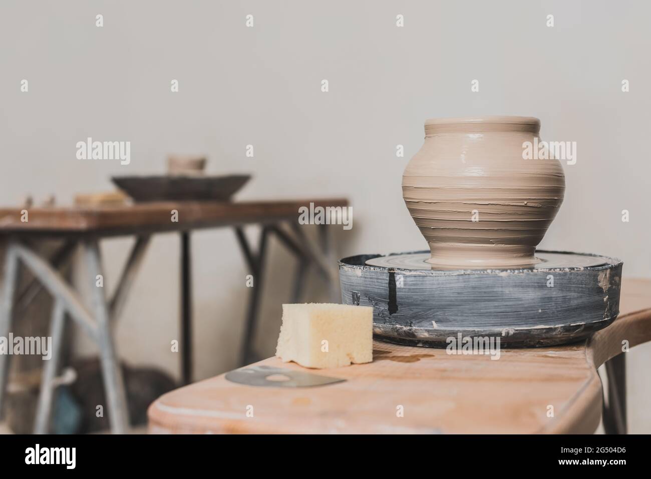 wet clay pot on pottery wheel and sponge on wooden bench in art studio ...