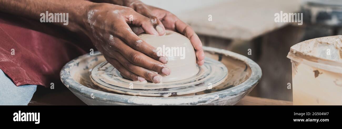 partial view of young african american man modeling wet clay on wheel ...