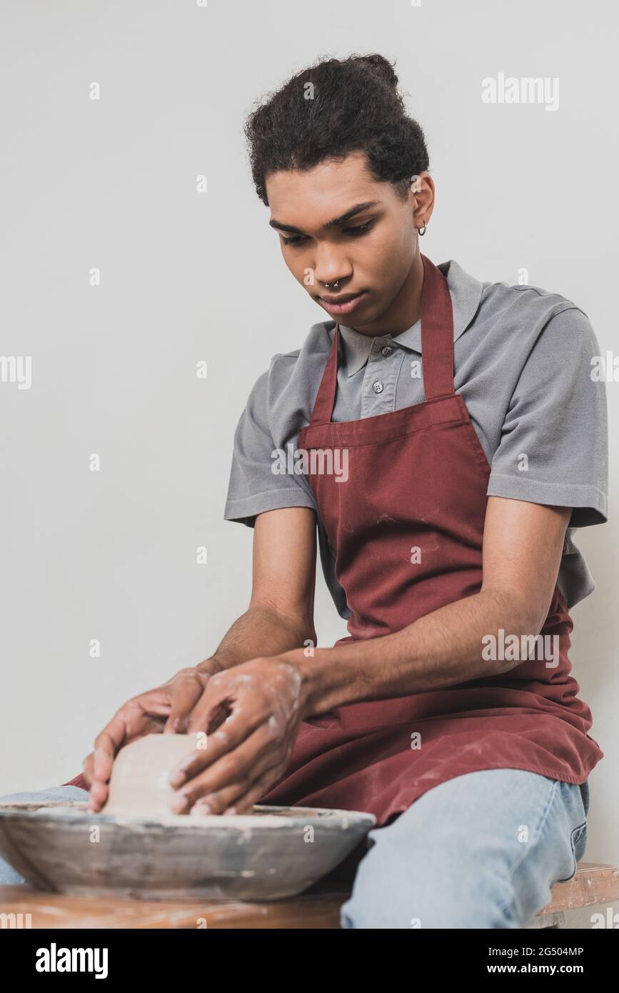 serious young african american man modeling wet clay on wheel with ...