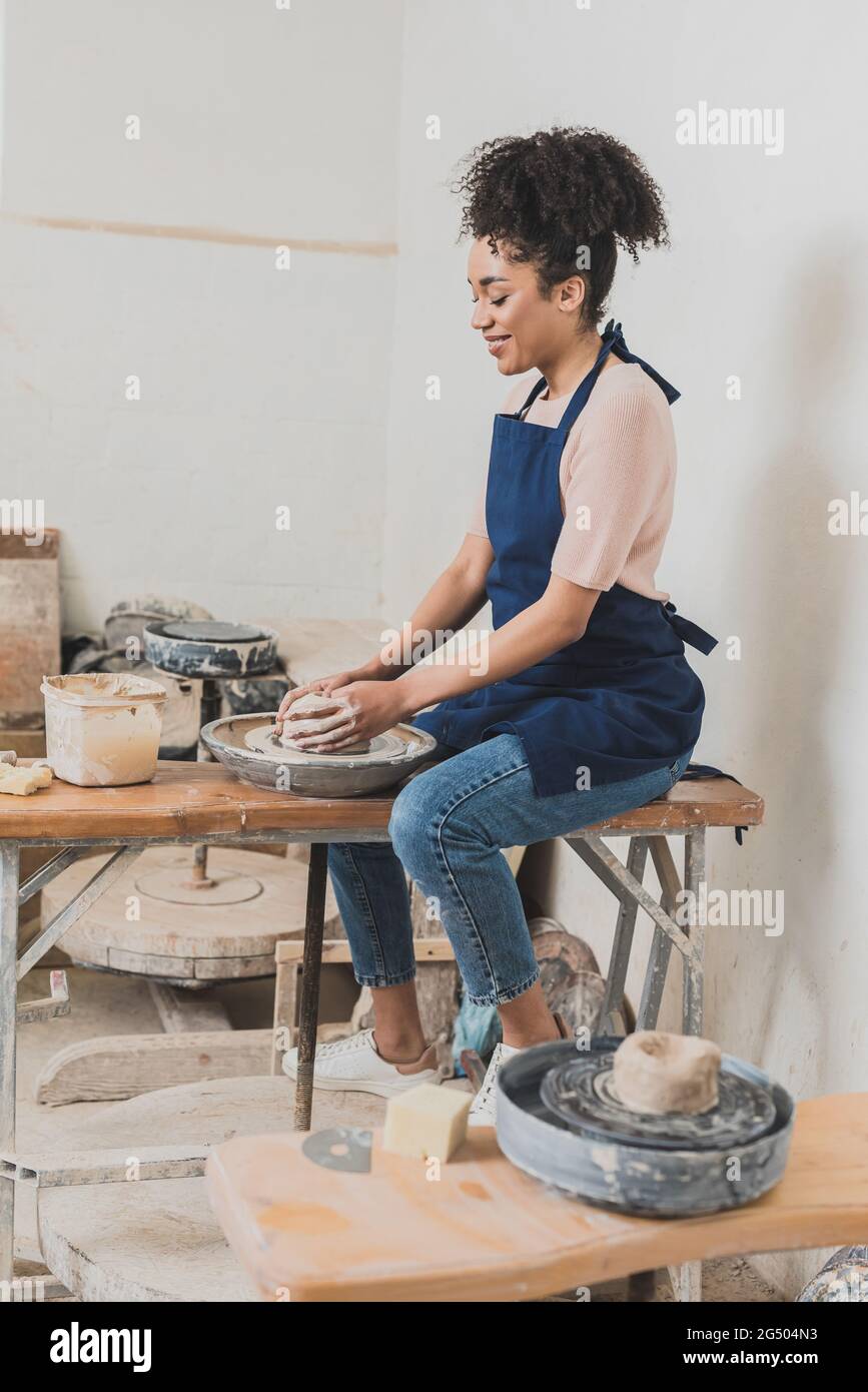 smiling young african american woman modeling wet clay on wheel with ...
