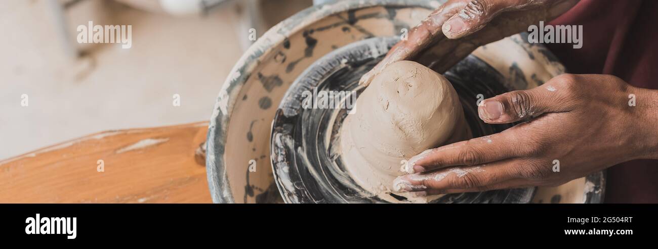 close up view of young african american man modeling wet clay on wheel ...
