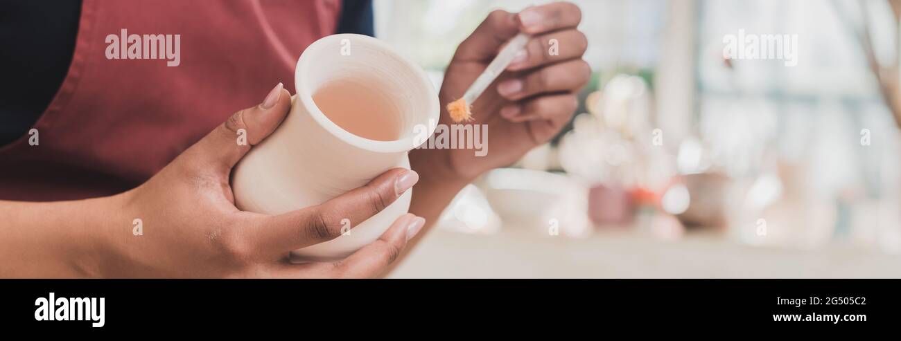 partial view of young african american woman glazing clay pot with ...