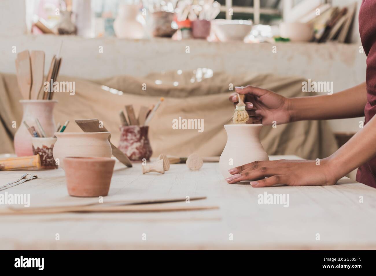partial view of young african american woman glazing clay pot with ...