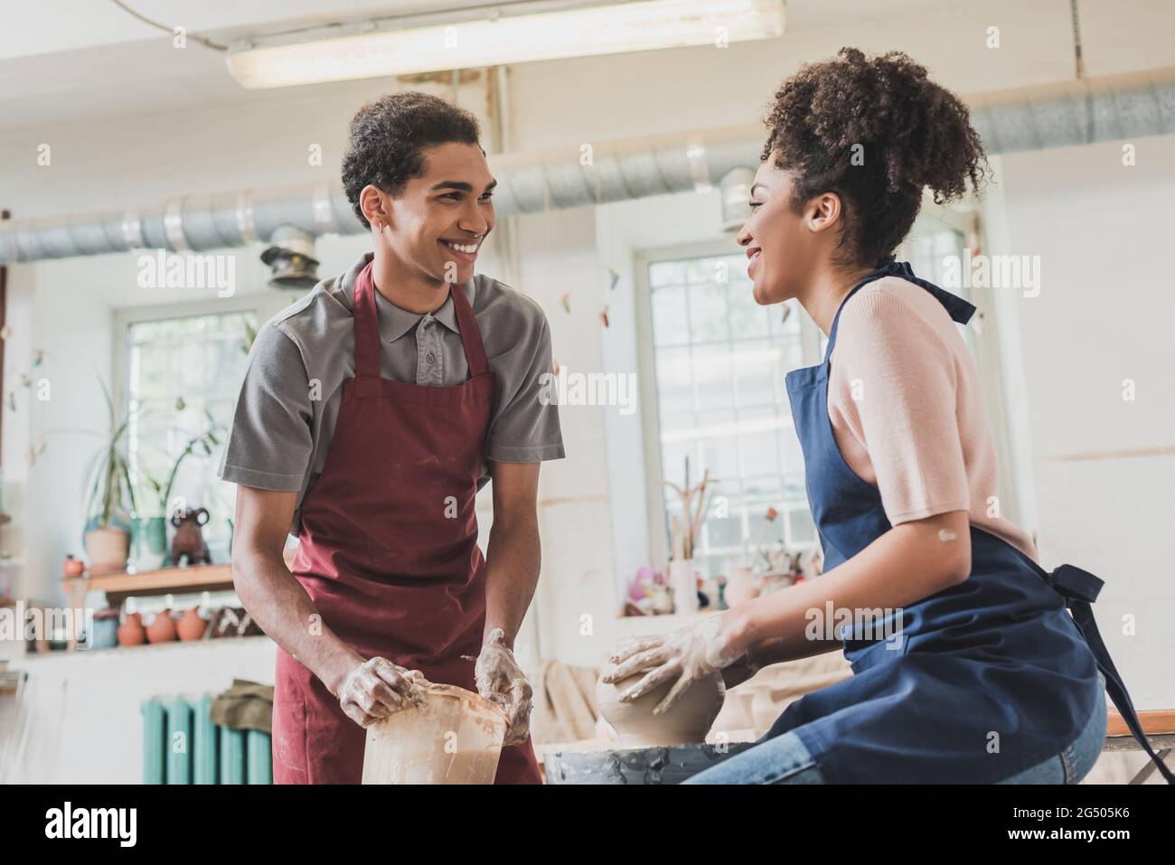 smiling young african american couple sculpting pot on wheel in pottery ...