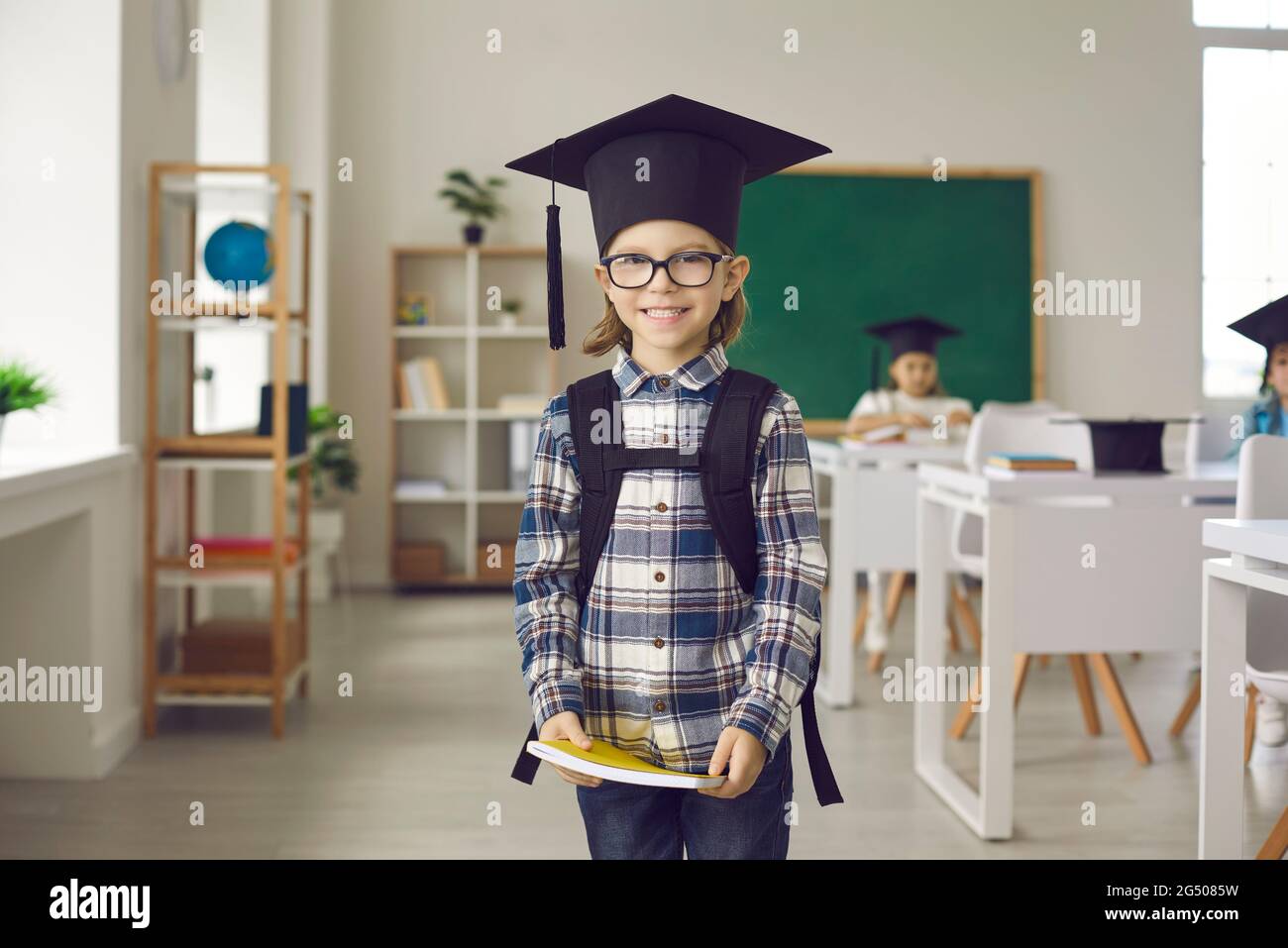 Portrait of happy elementary school kid in academic hat and glasses ...