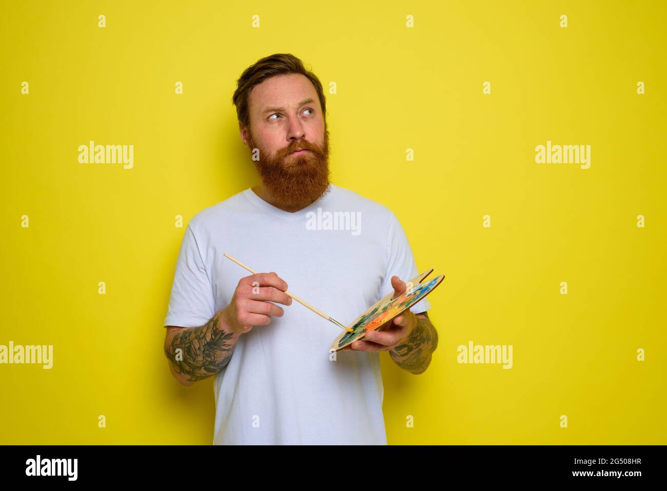 Undecided man with beard and tattoo is ready to draw with brushes Stock ...