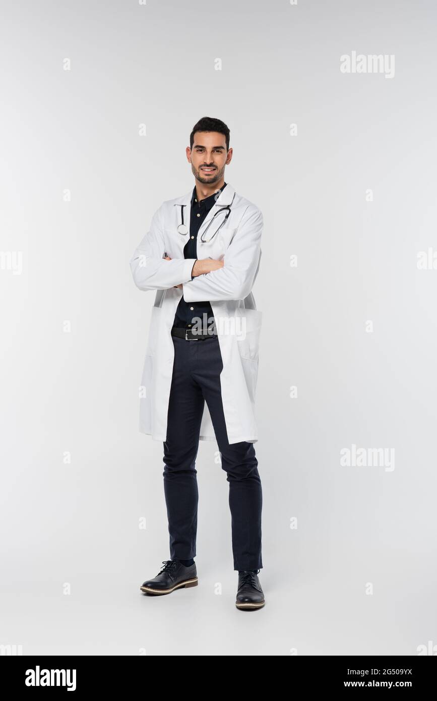 Smiling arabian doctor standing with crossed arms on grey background ...