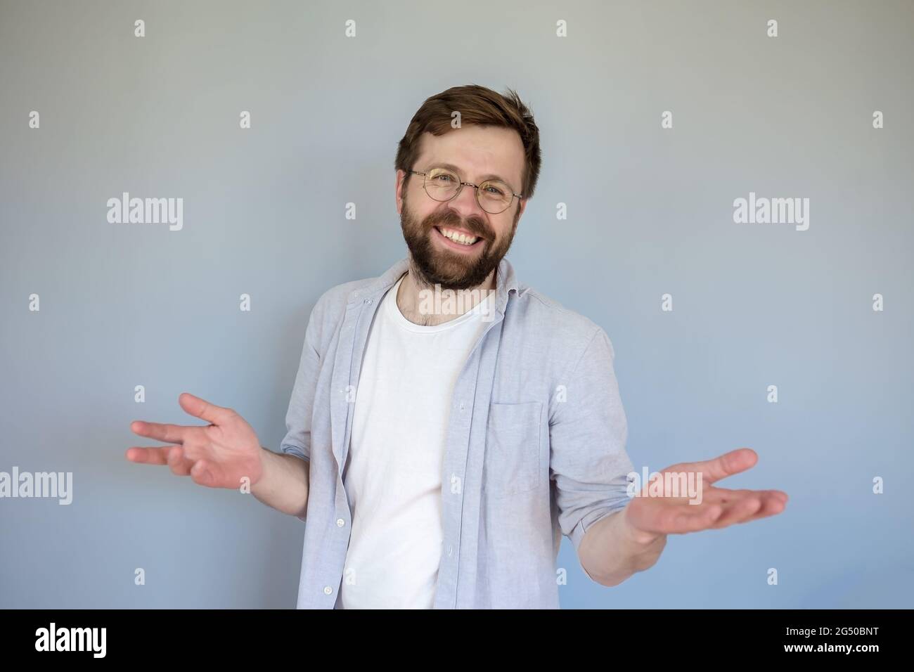 Friendly, charming man smiles cute and makes a gesture with hands. Gray ...