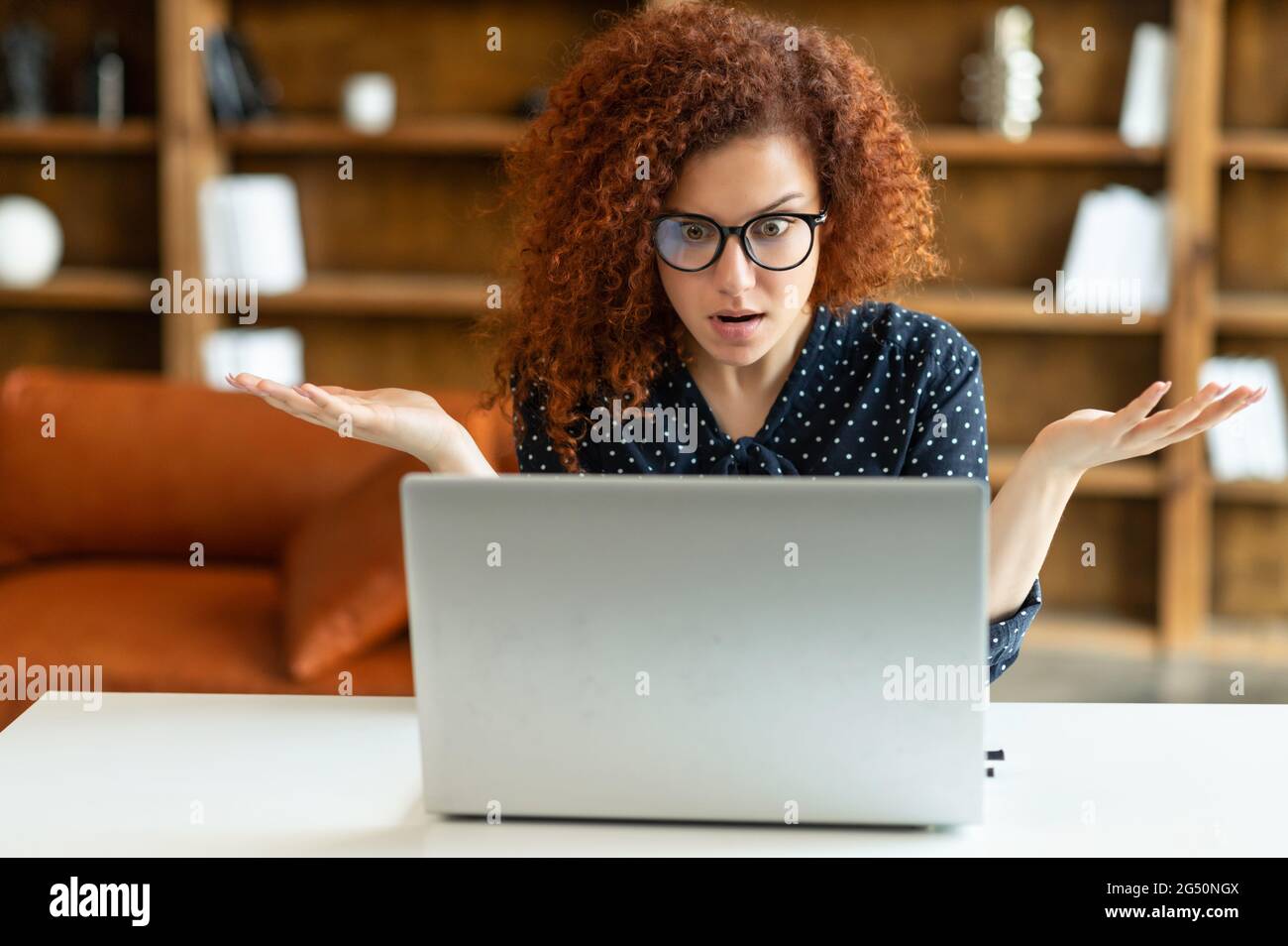 Puzzled and confused redhead female entrepreneur staring at the laptop ...