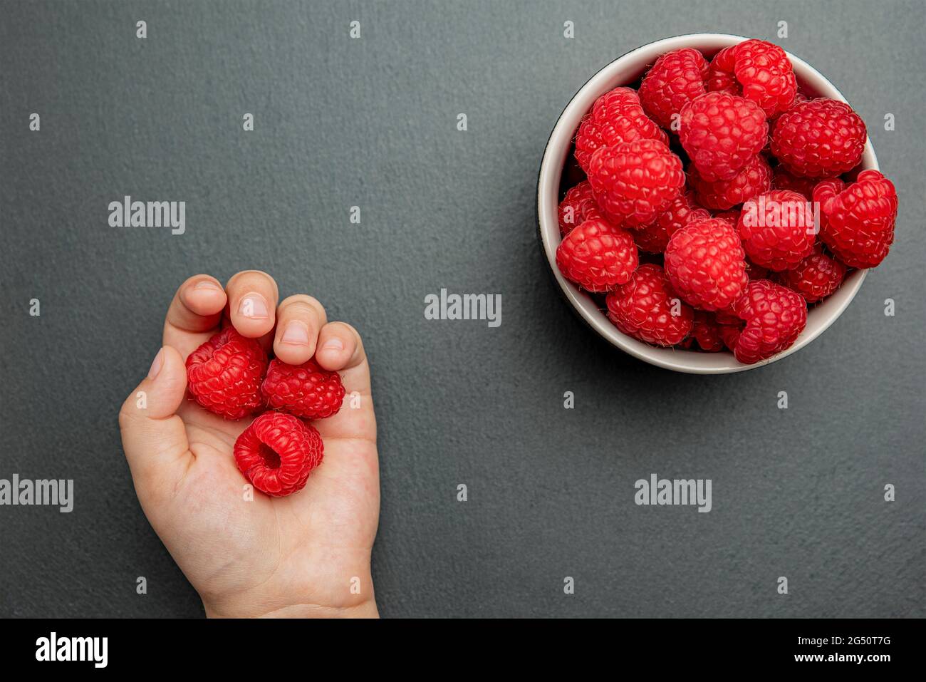 Raspberries in a saucer on a black background. The child takes ...