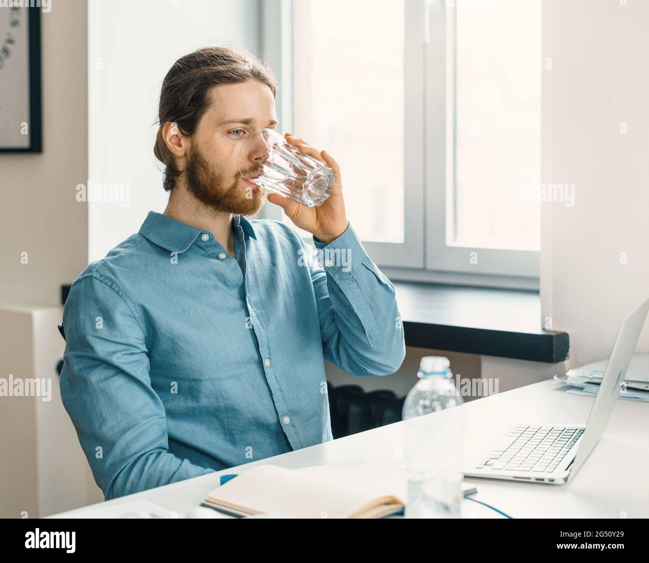 Young man drinking pure mineral water while working on laptop Stock ...