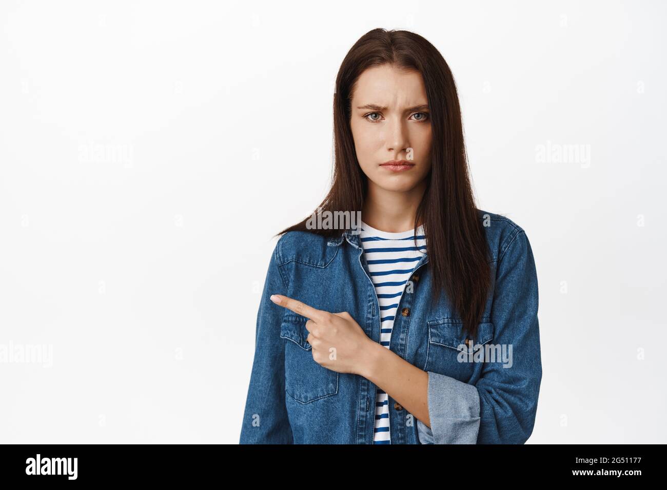 Portrait of concerned young woman frowning, pointing left with hesitant ...