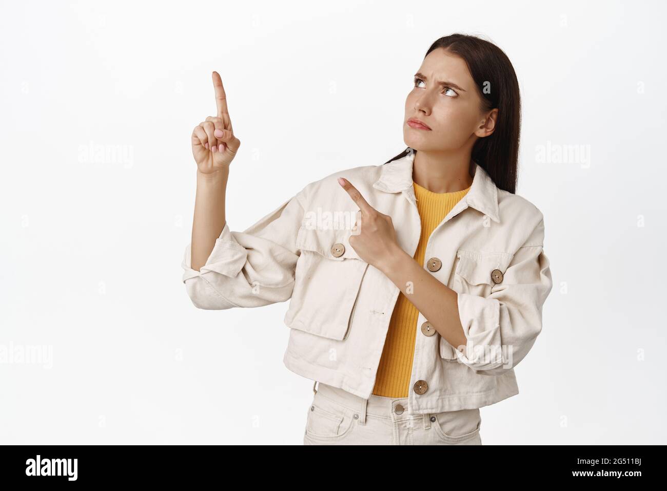 Skeptical woman furrow eyebrows, pointing and looking at upper left ...