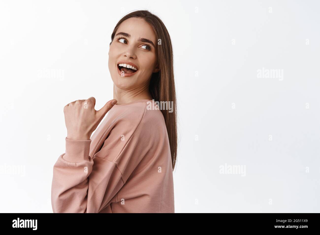 Portrait of cheerful beautiful girl pointing thumb and look behind her ...