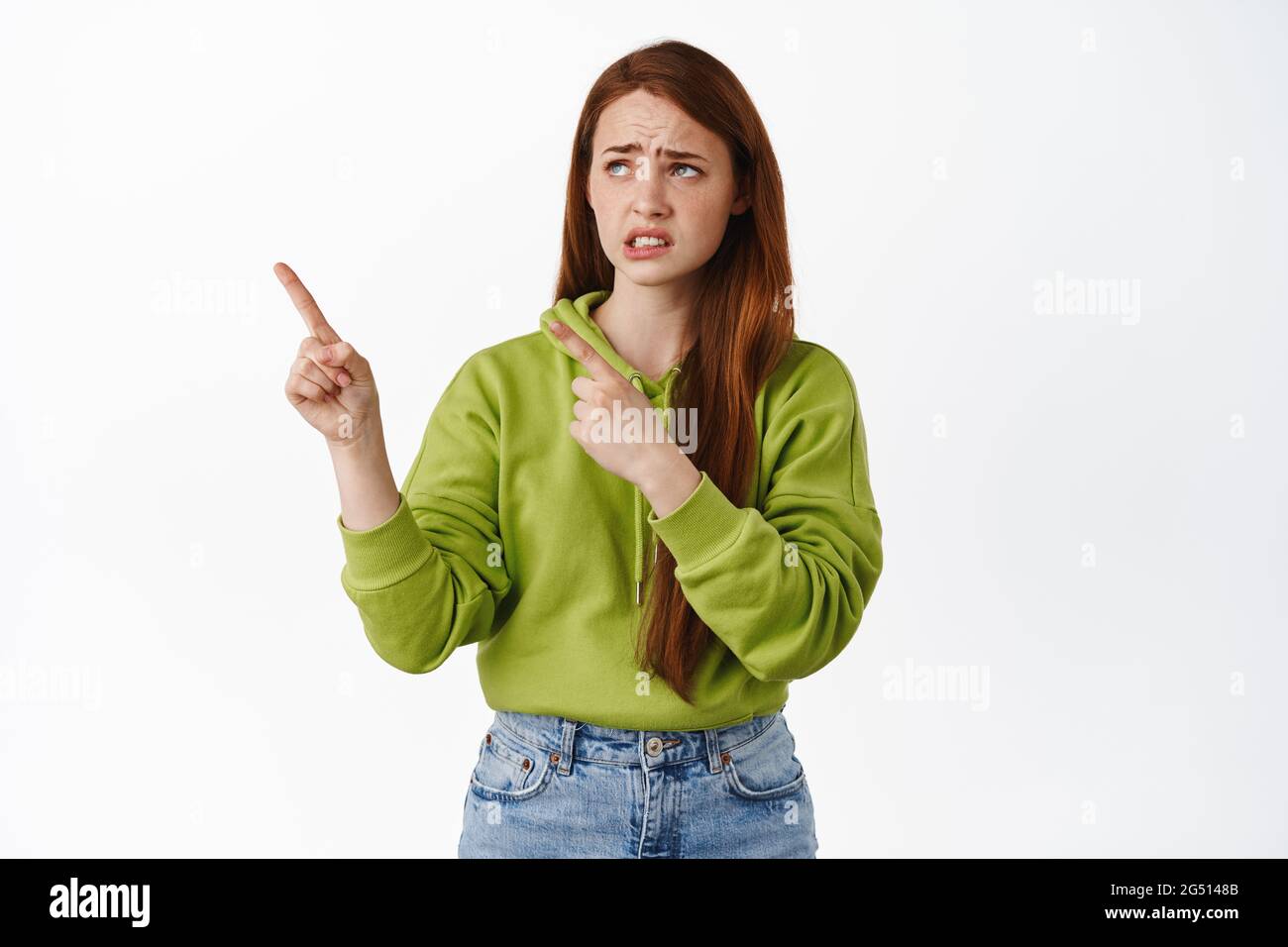 Awkward and unsure redhead woman, pointing and looking at upper left ...