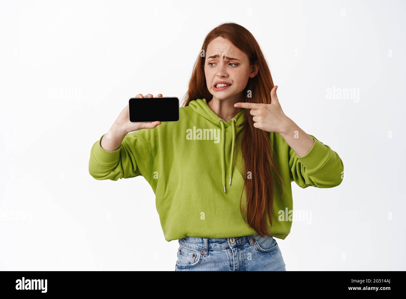 Worried ginger girl pointing at horizontal phone screen, has concern ...