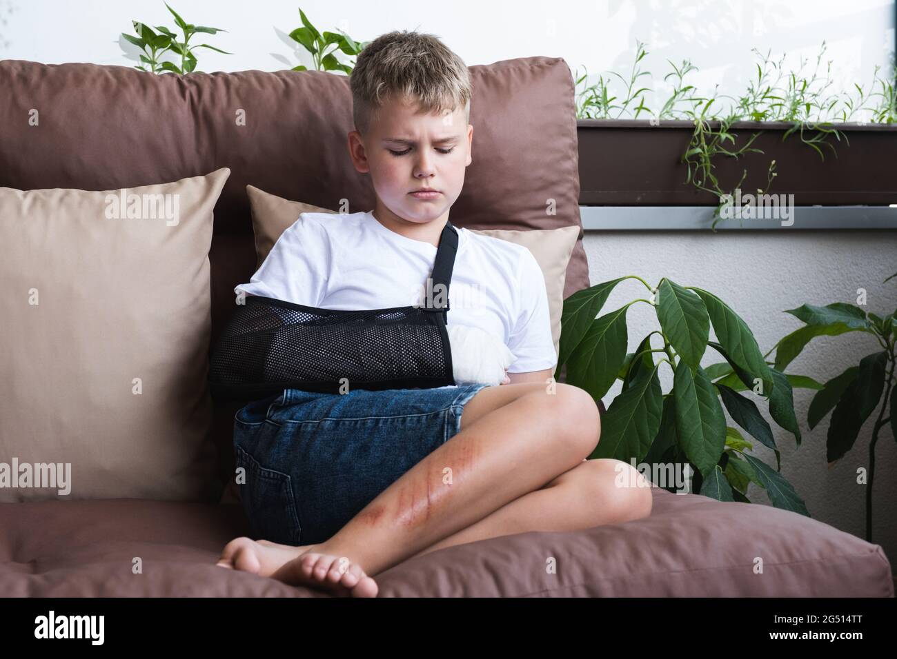 Sad boy with a broken arm and wounds on his leg. Gypsum on a child's ...