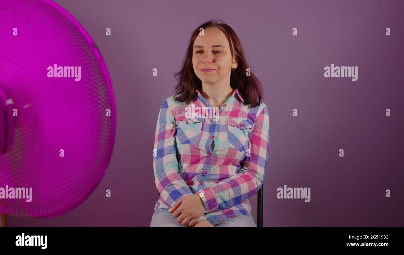 Close up of young woman sitting on chair in front of fan on purple ...
