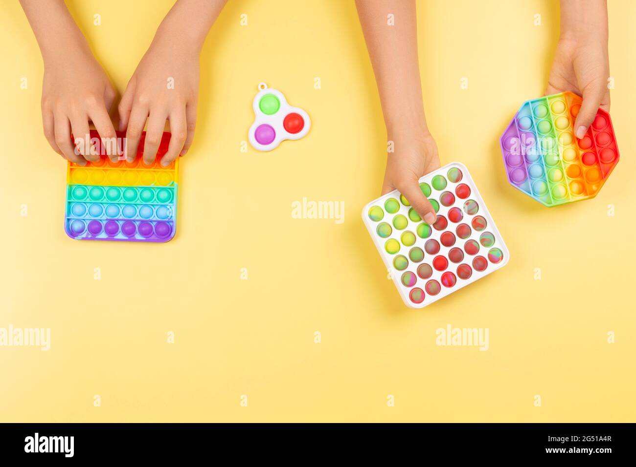 Many hands holding pop it fidget toys on yellow background. Push pop-it ...