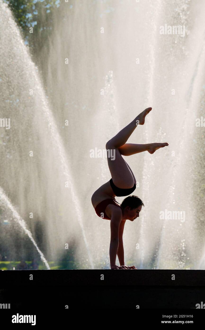 Silhouette of woman doing acrobatic handstand pose against fountain ...