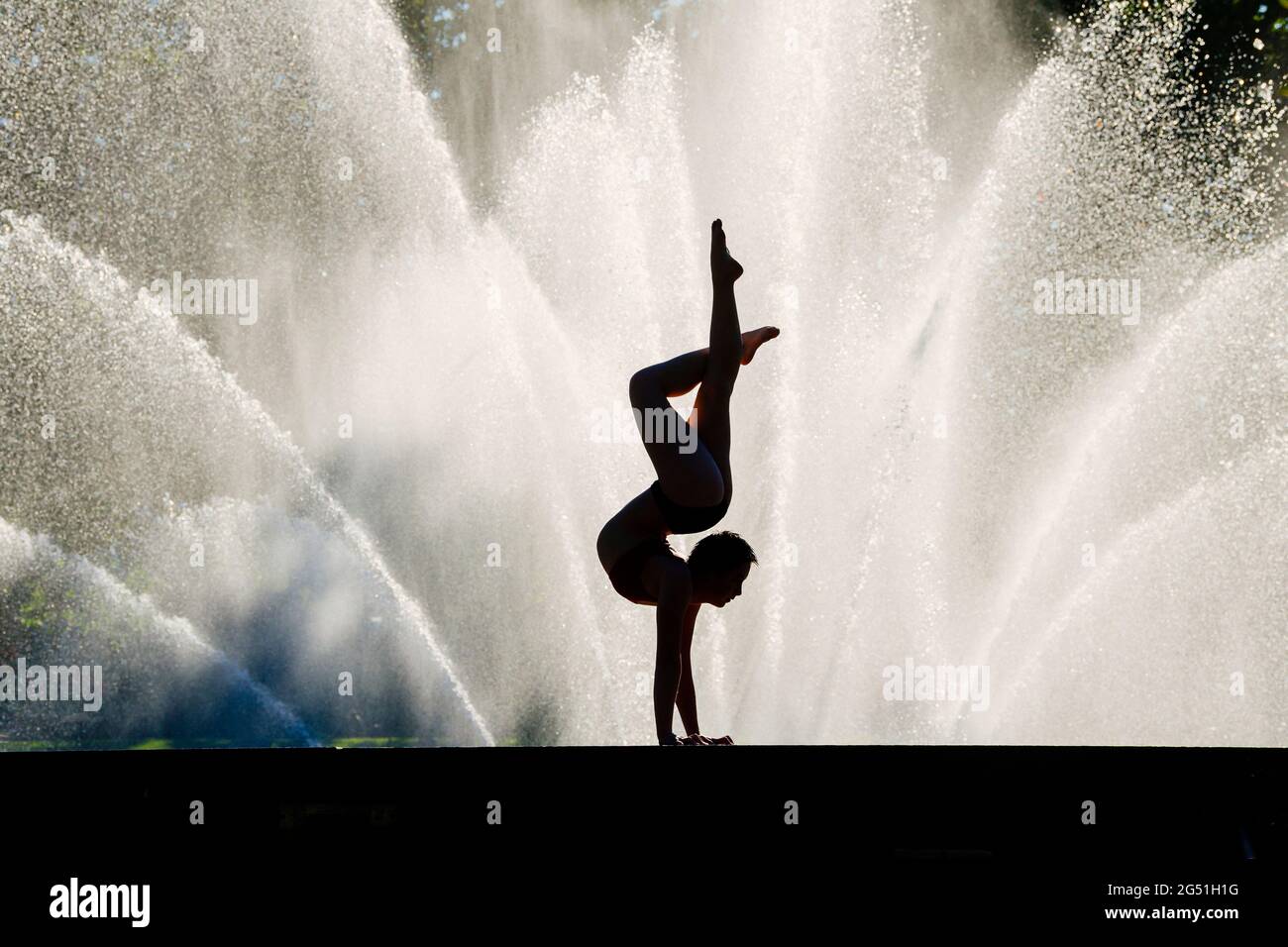 Silhouette of woman doing acrobatic handstand pose against fountain ...