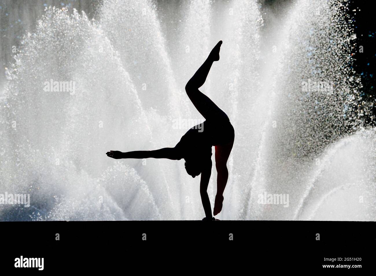 Silhouette of woman doing acrobatic handstand pose against fountain ...