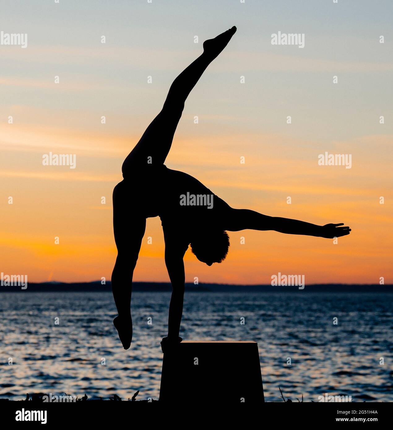 Silhouette of woman doing acrobatic pose against sea at sunset Stock ...