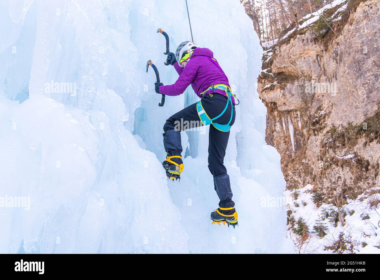 Woman climbing down the side of an icy slope, hanging on a rope ...