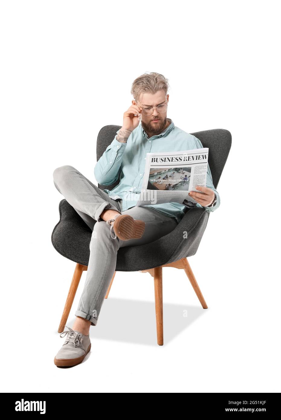 Young man reading newspaper while sitting in armchair on white ...
