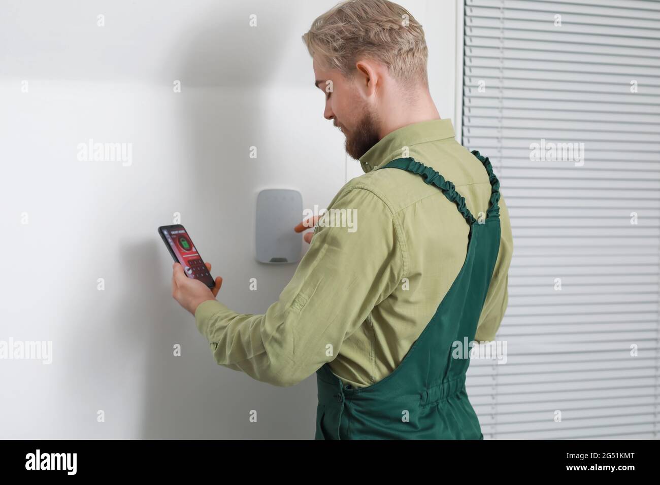 Worker with smartphone checking alarm system indoors Stock Photo - Alamy