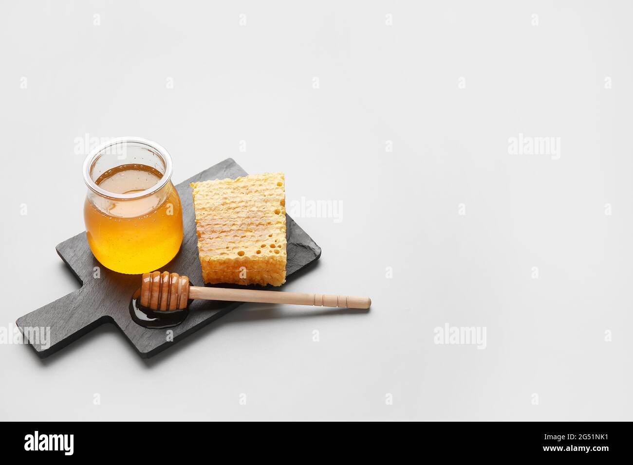 Glass jar with sweet honey, comb and dipper on board against grey ...