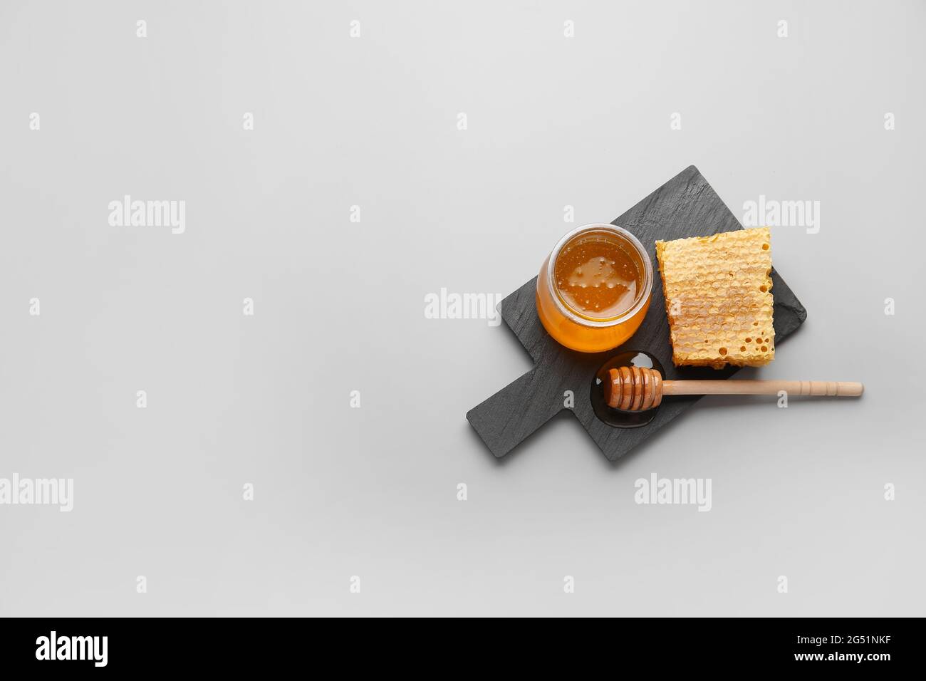 Glass jar with sweet honey, comb and dipper on board against grey ...