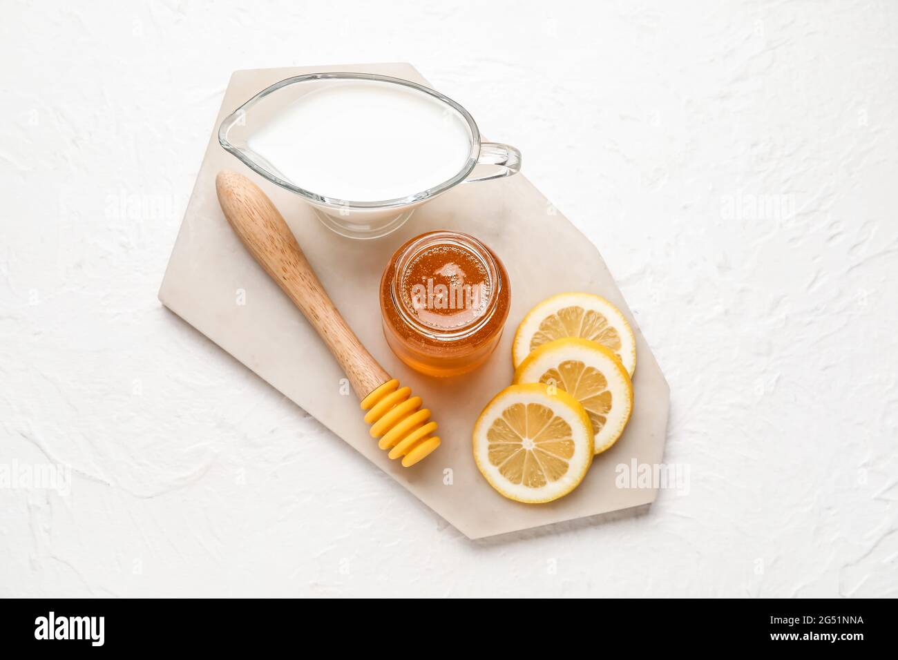 Glass jar with sweet honey, dipper, lemon slices and jug of milk on ...