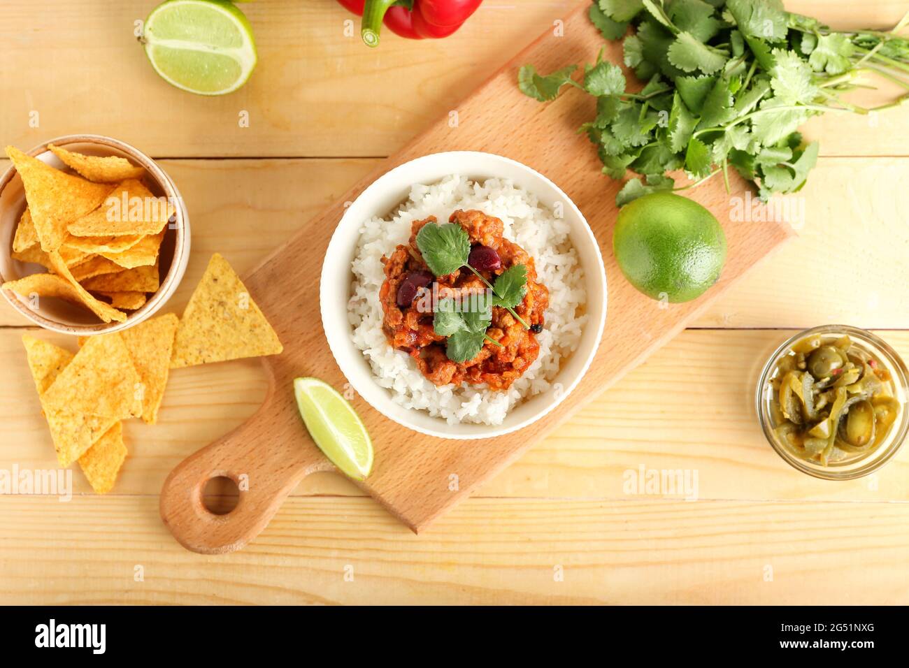 Bowl with tasty chili con carne, rice, lime and nachos on wooden ...