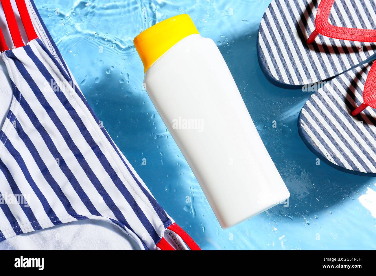 Bottle of sunscreen, flip-flops and swimsuit on color background with ...