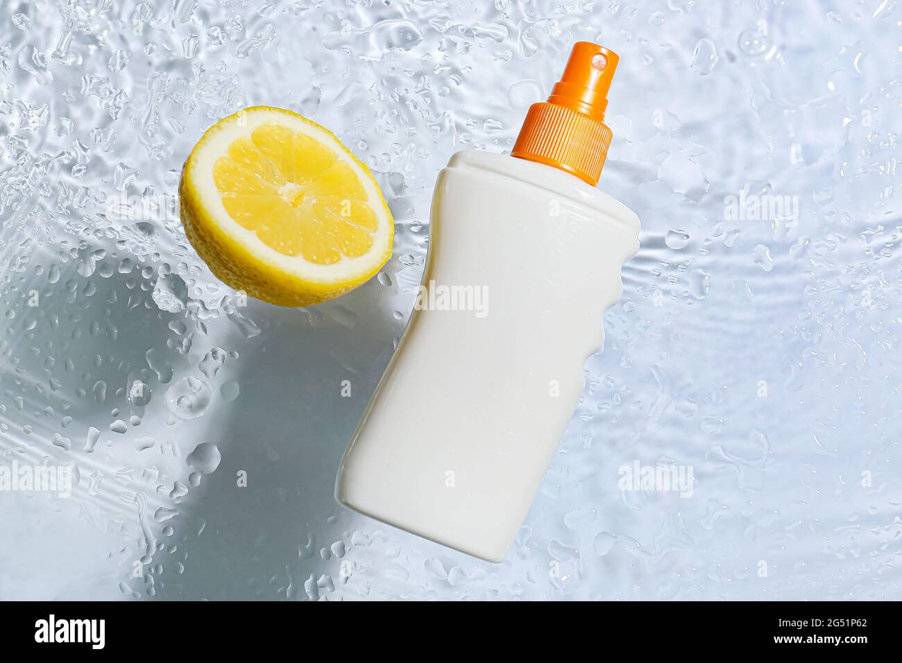 Bottle of sunscreen and lemon on light background with water drops ...